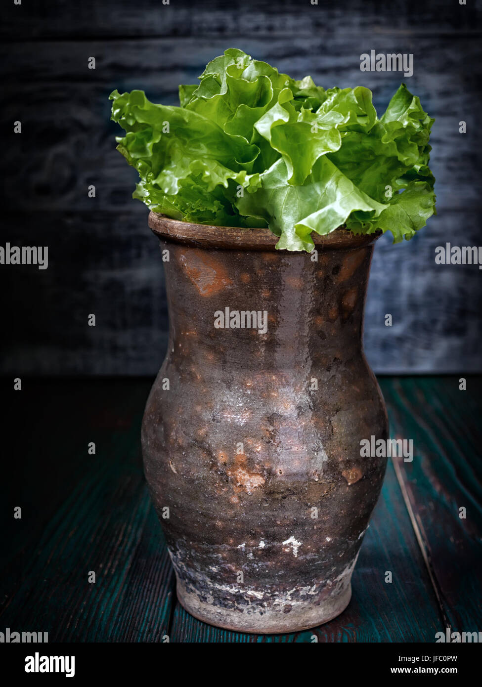 Lettuce leaves in ancient jug on wooden background, brick wall, style ...