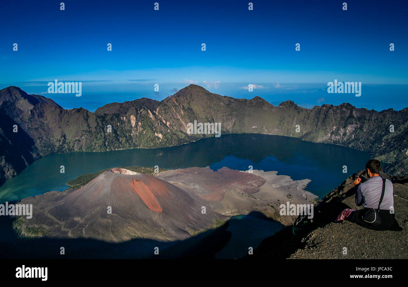 Tourist sitting on the rim of the crater of Gunung Rinjani volcano in ...