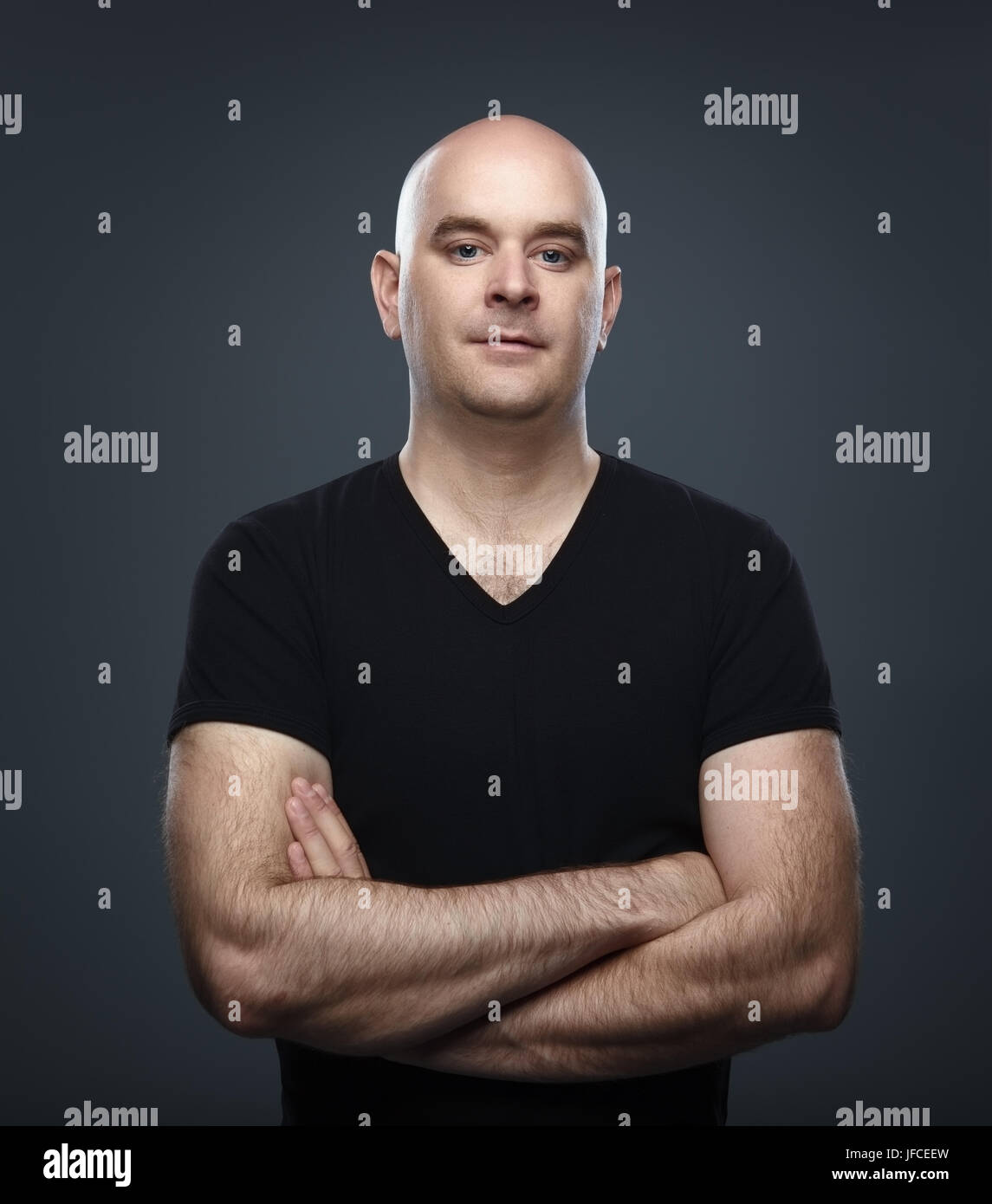 Bald man crossed his arms over his chest in a black T-shirt. Studio ...