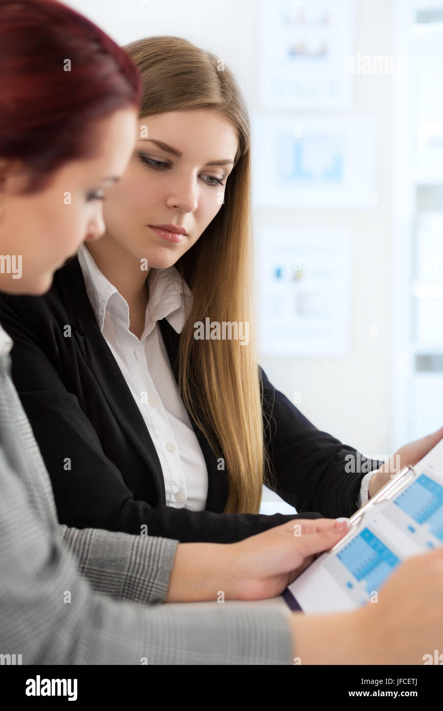 Two woman sitting at office and looking at charts and tables discussing ...