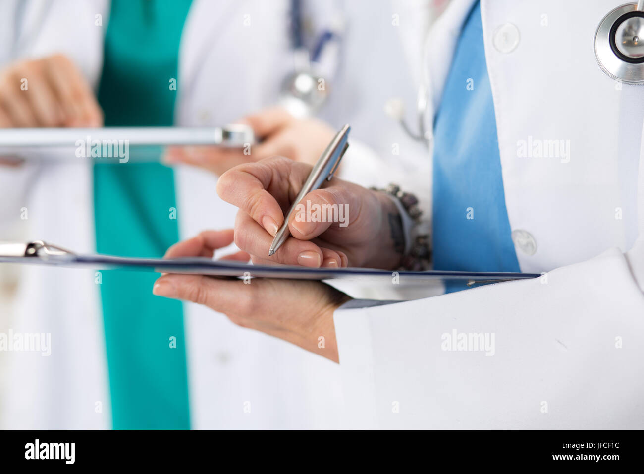 Close up view of medical doctor hands making some notes on clipboard ...