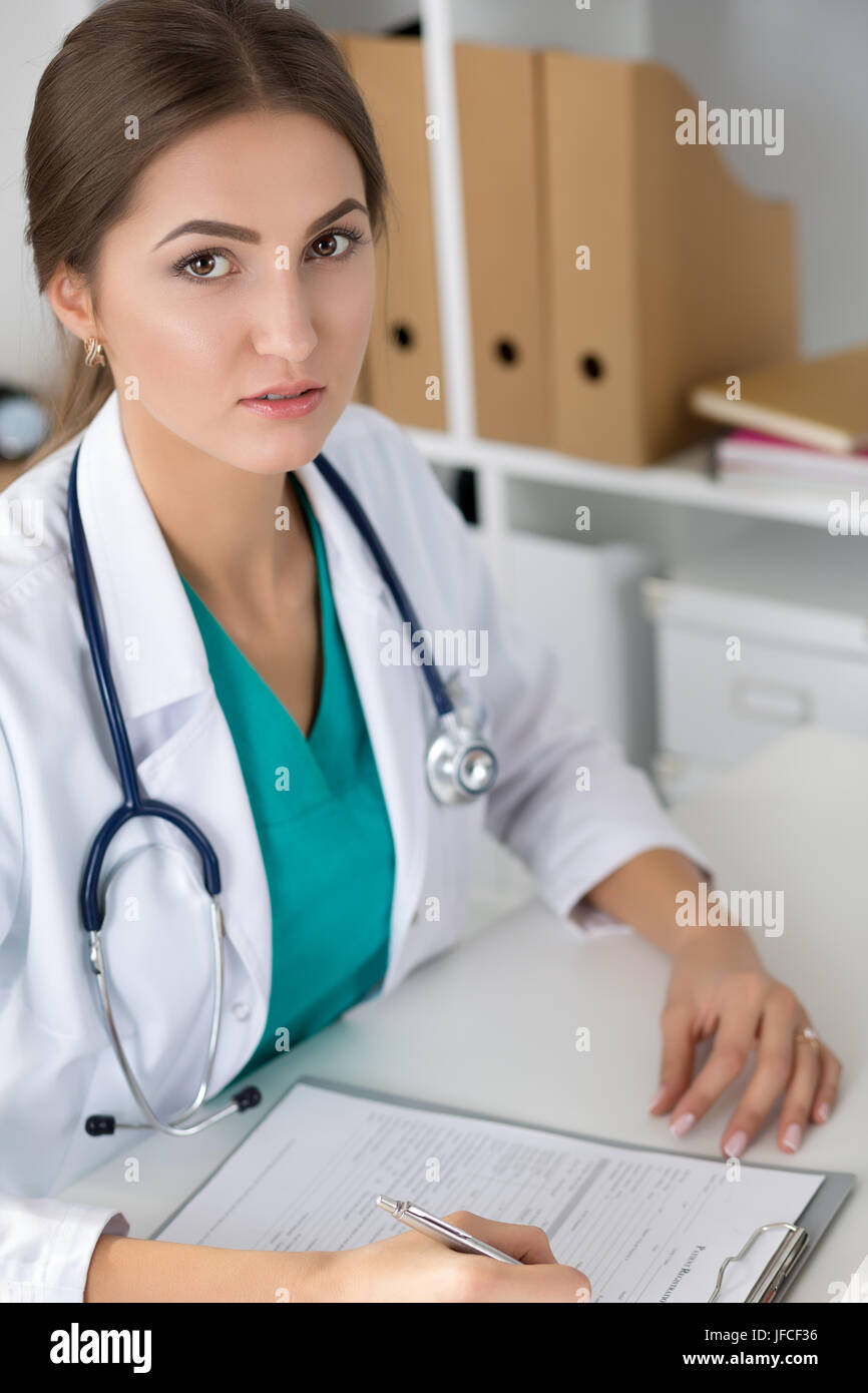 Portrait of female medicine doctor filling patient medical form at her ...
