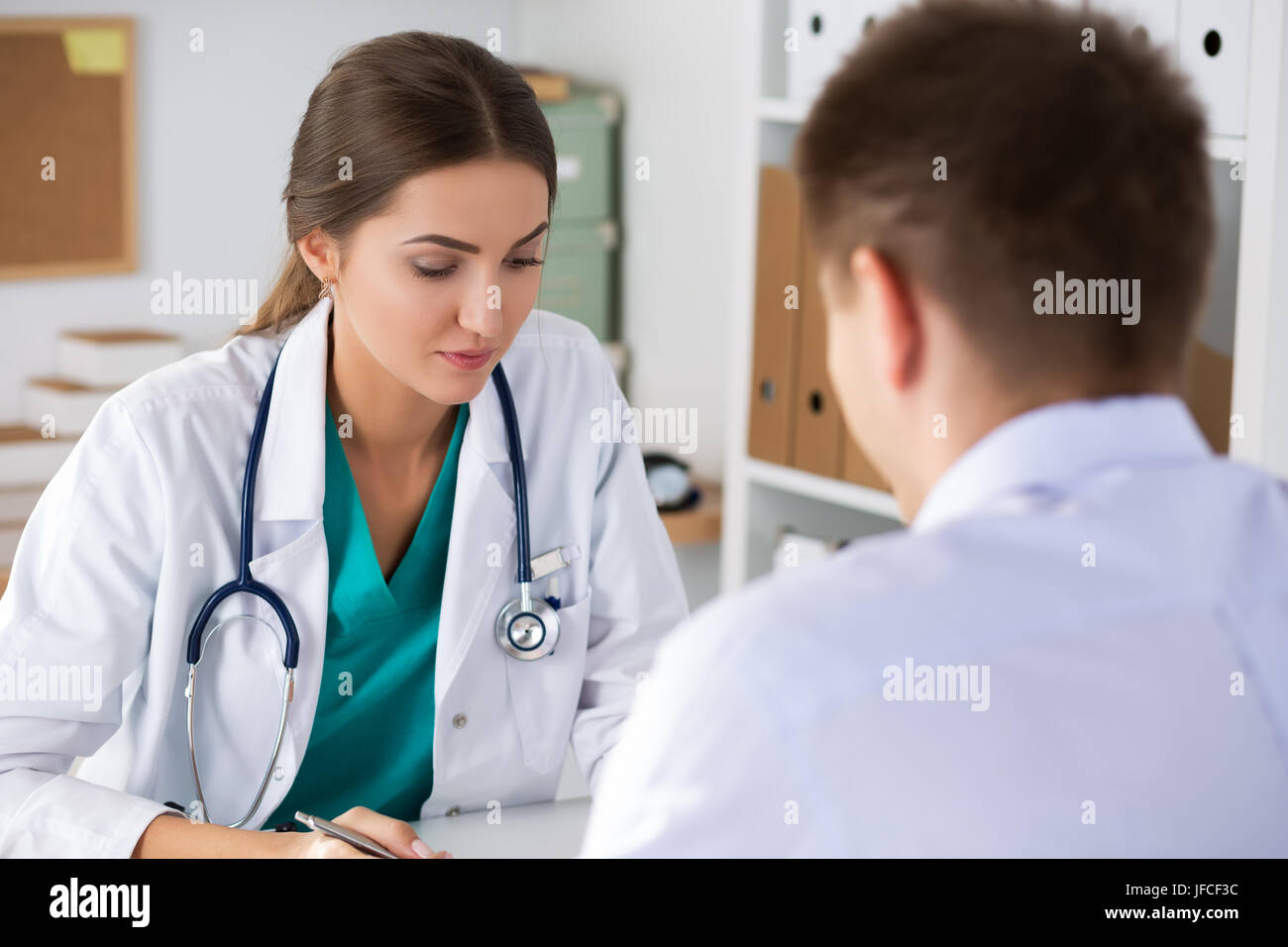 Female doctor writing prescription to her male patient or conculting to ...