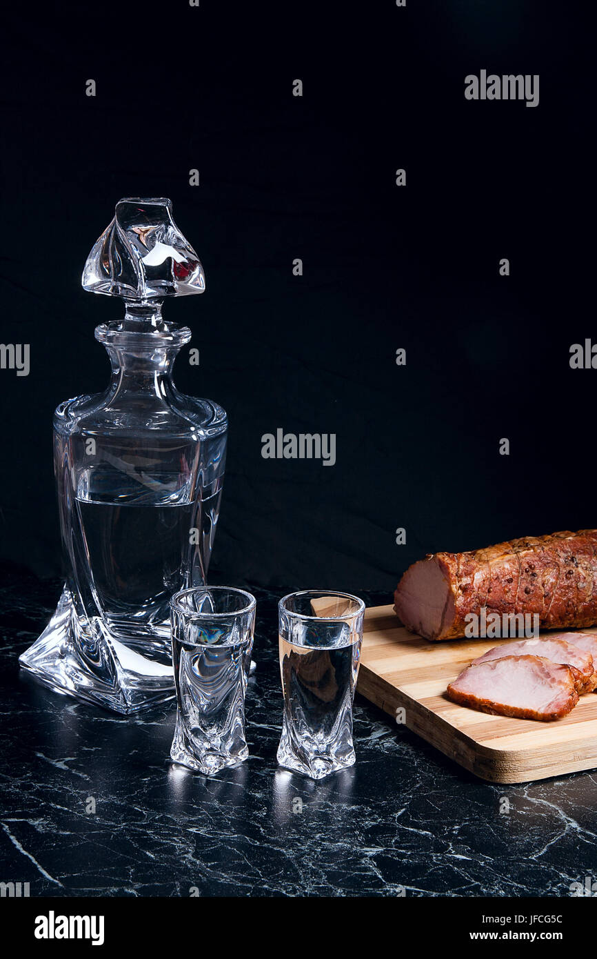Bottle and shot glasses with vodka. Slices of smoked meat or ham on ...