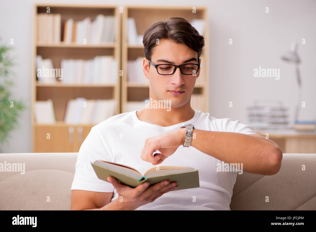 Man reading book sitting in couch sofa Stock Photo - Alamy