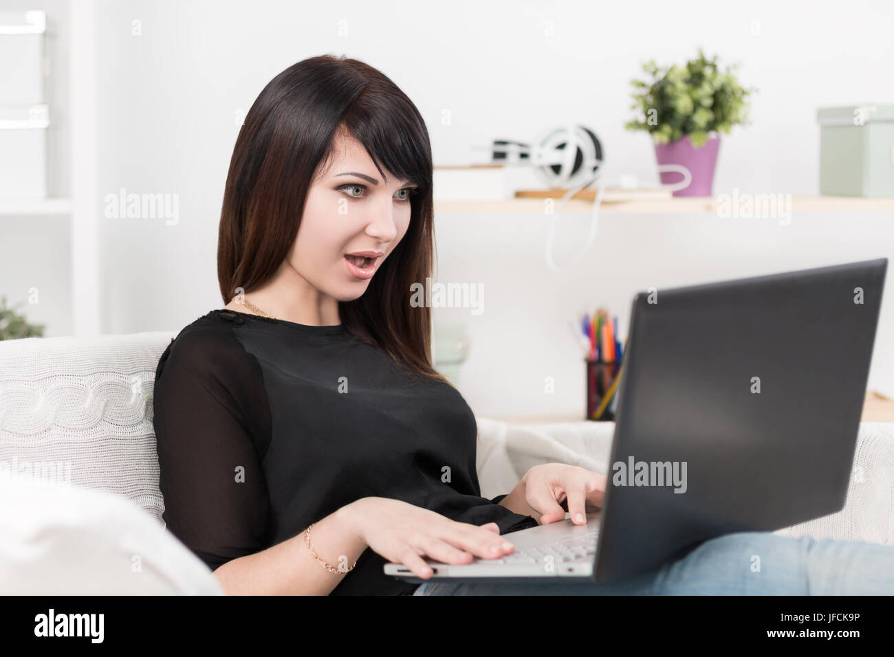 Portrait of young shocked woman sitting in front of laptop computer ...