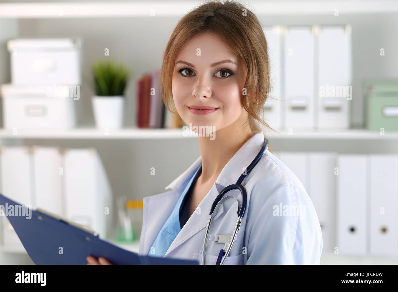 Smiling female medicine doctor filling in patient medical history list ...