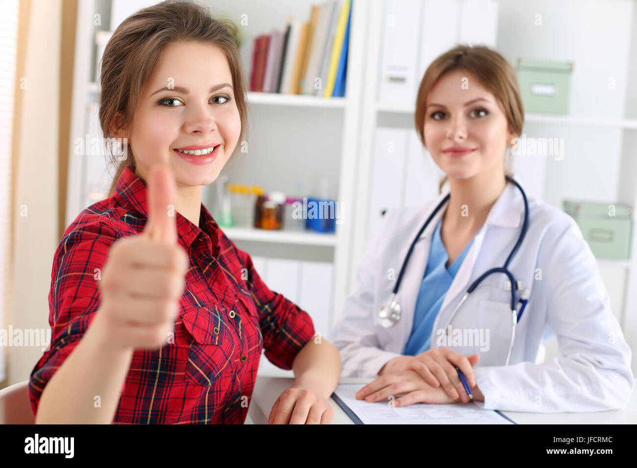 Smiling female patient showing OK sign with thumb up sitting at doctor ...