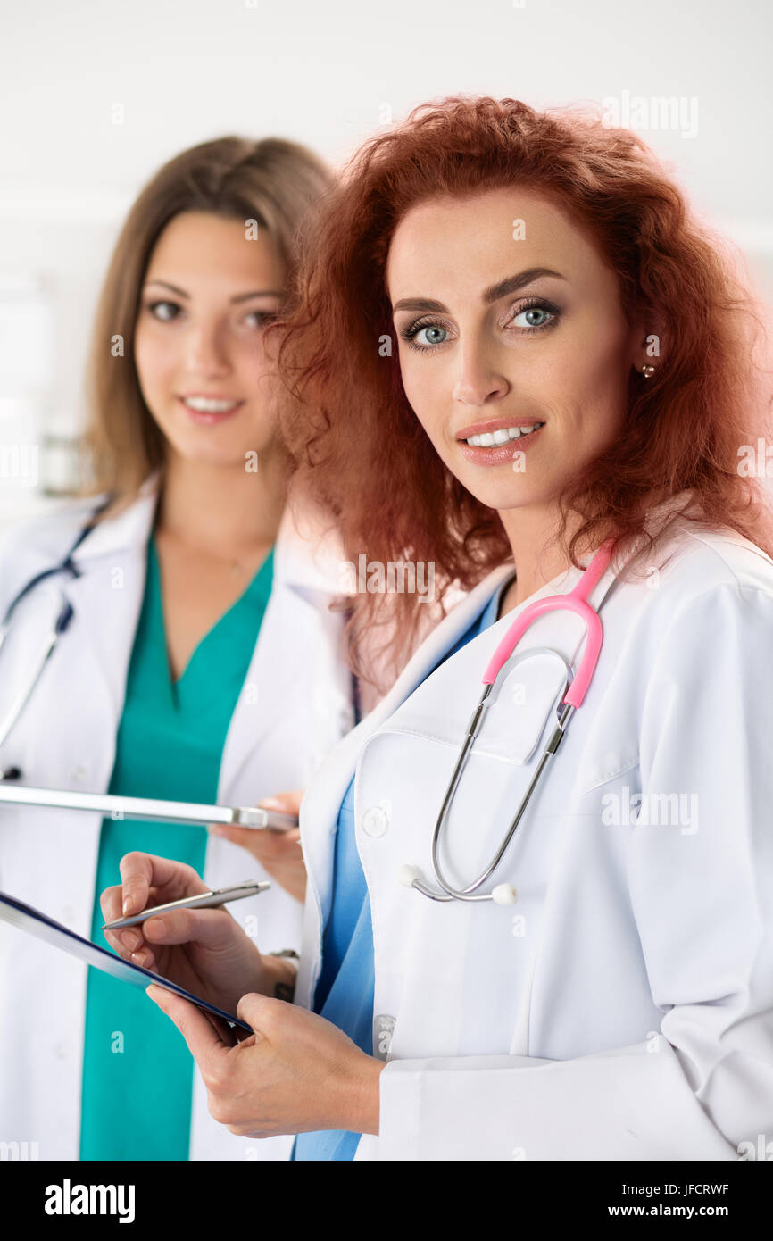 Portrait of two female doctors standing with clipboard and tablet ready ...