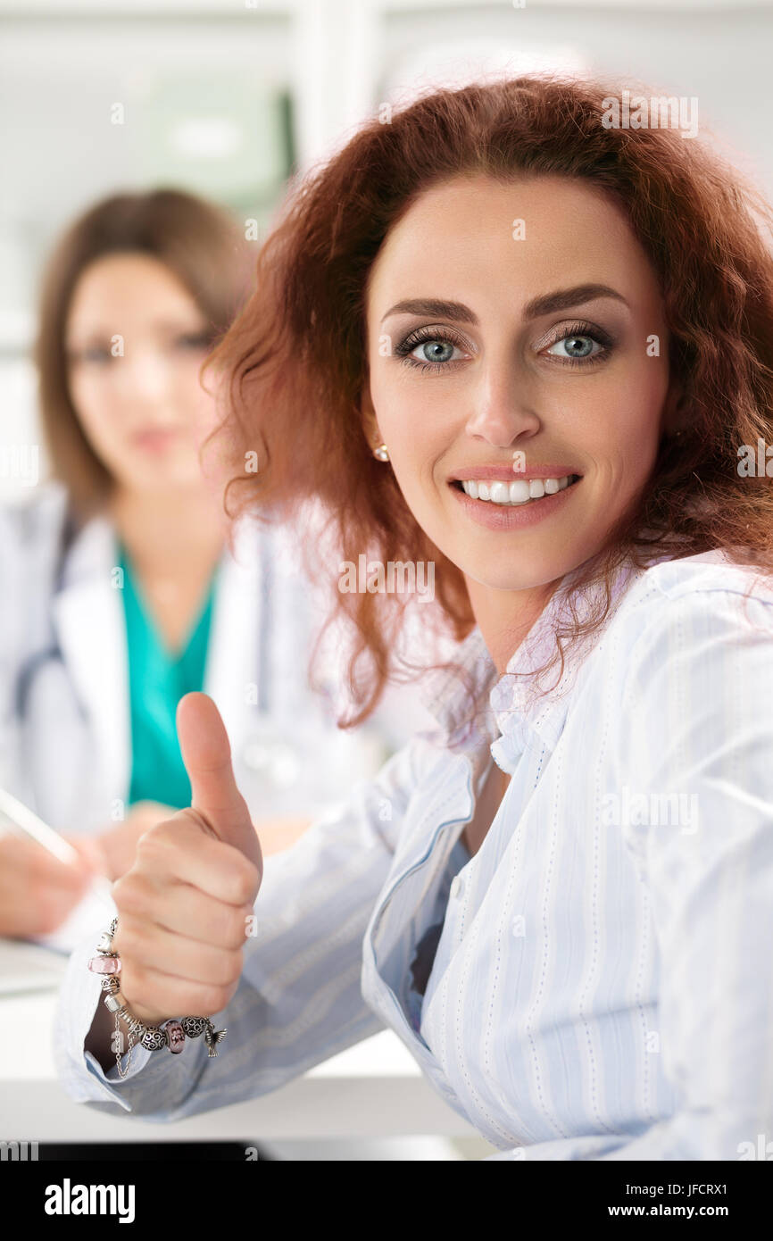 Smiling female patient showing OK sign with thumb up at medical doctor ...