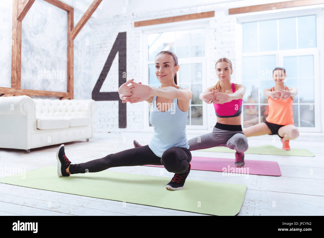 Very intensive. Three young pretty ladies doing squats at modern light ...