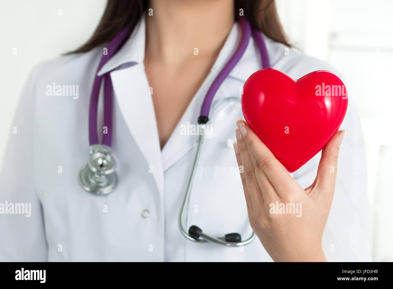 Female doctor's hands holding red heart in front of her chest. Doctor's ...