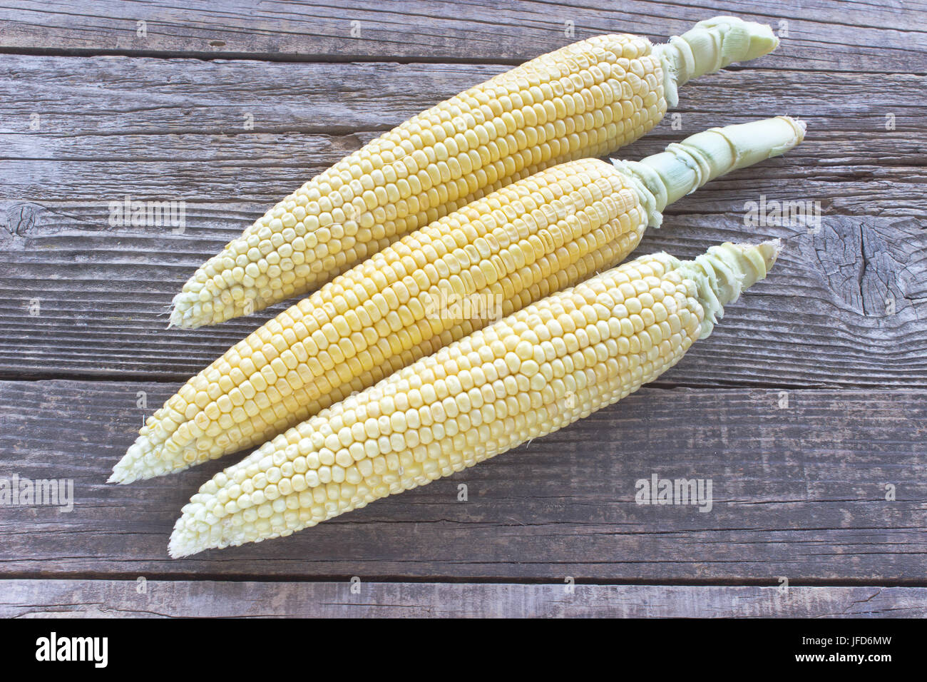 Three corn cobs on wooden background Stock Photo - Alamy