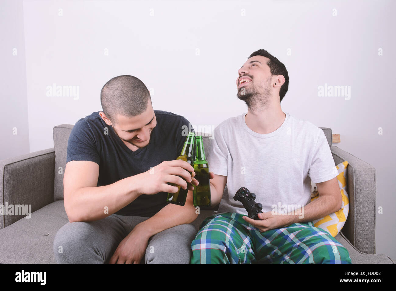 Portrait of two friends playing videogames, eating snacks and drinkng ...