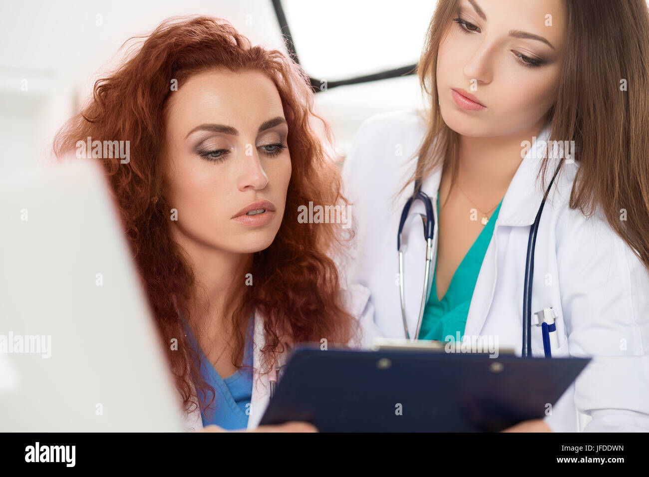 Two female doctors looking at clipboard with patient information form ...