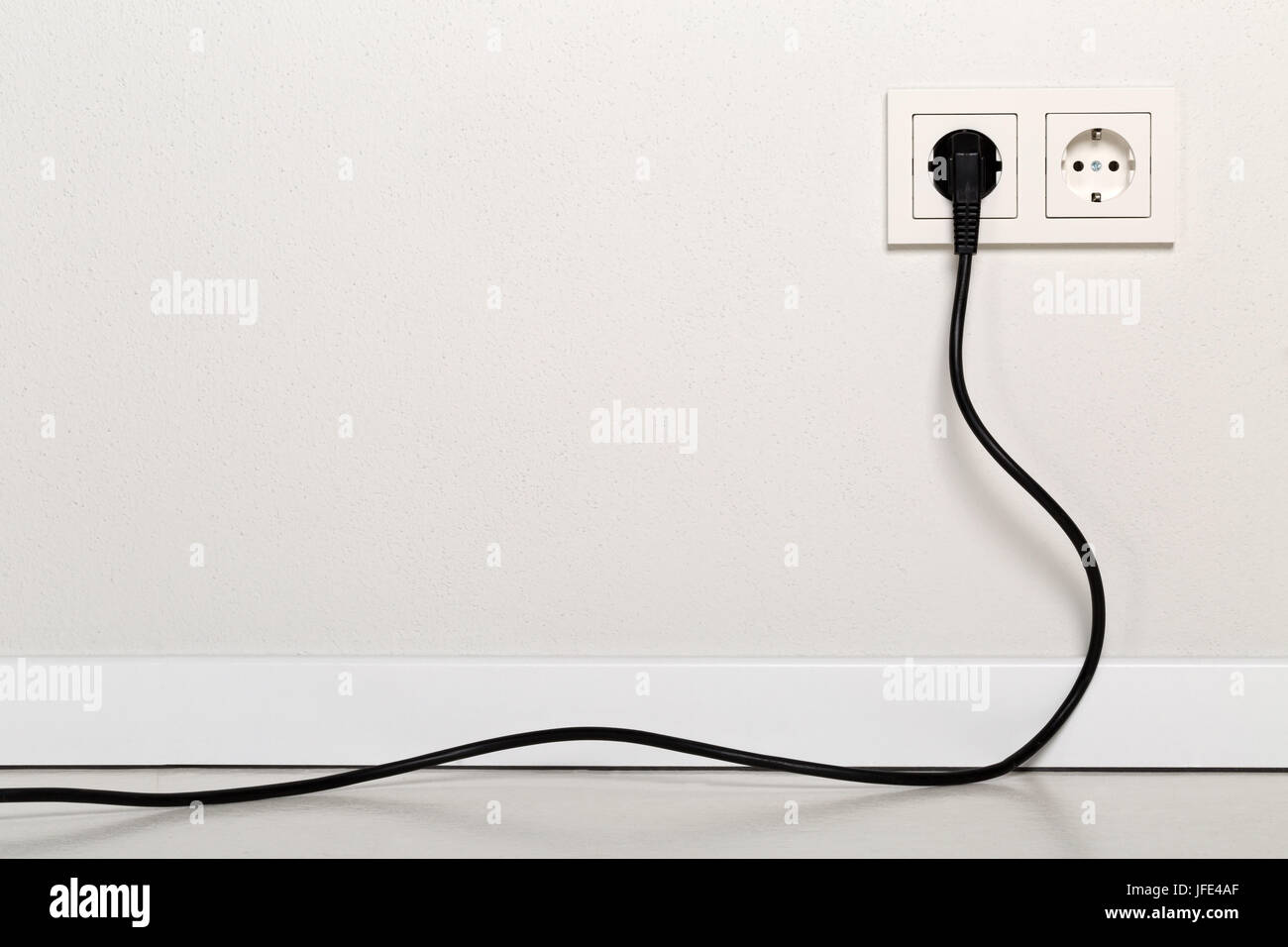 Black power cord cable plugged into european wall outlet on white ...