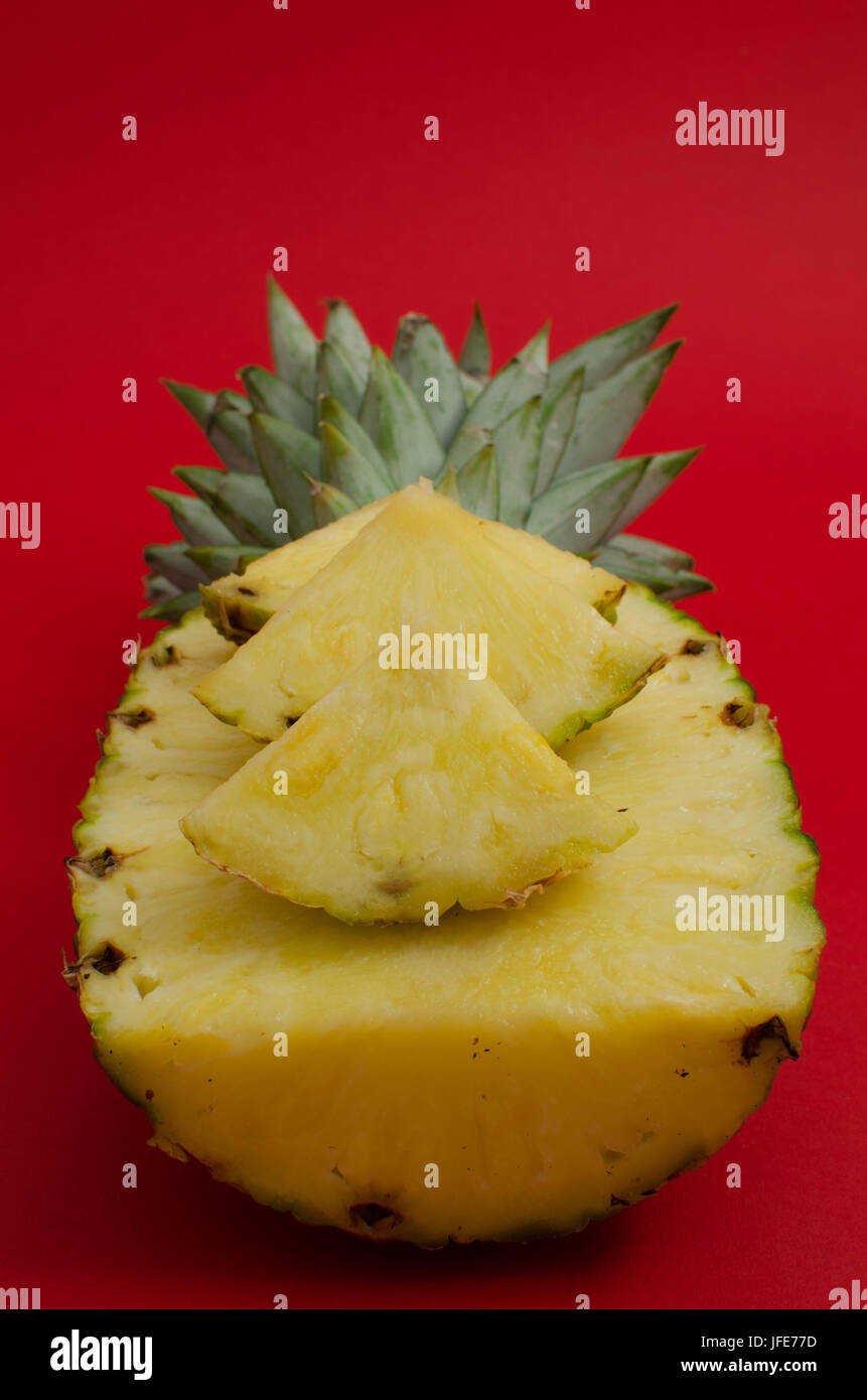 sliced pineapple fruit on red background, half of fruit with triangles ...