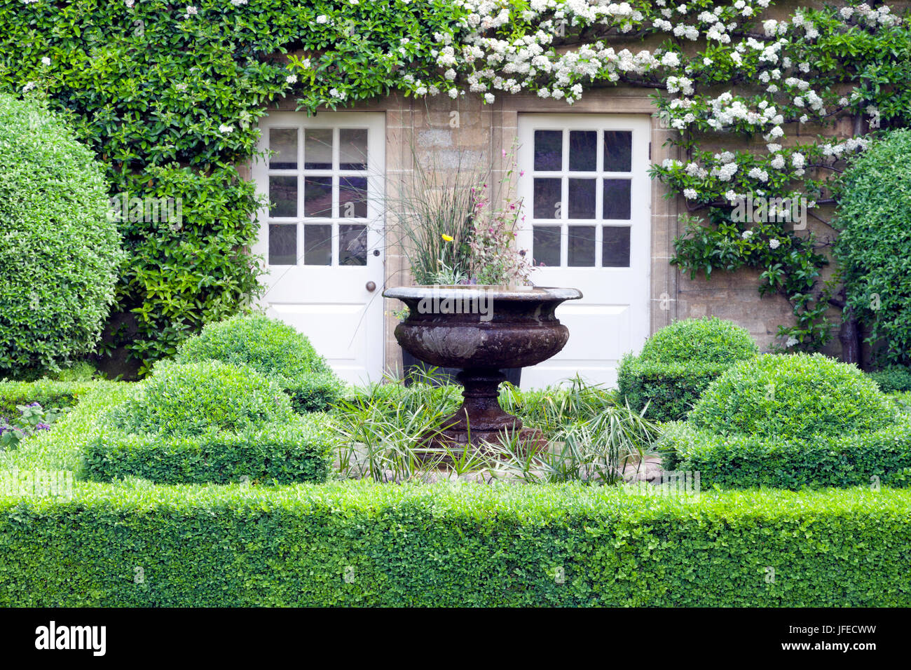 Flower vase in green topiary garden in front of a stone English country ...