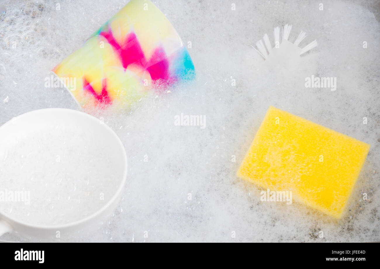 Colorful dirty mug, white cup, sponge and a brush soaking in foamy soap ...