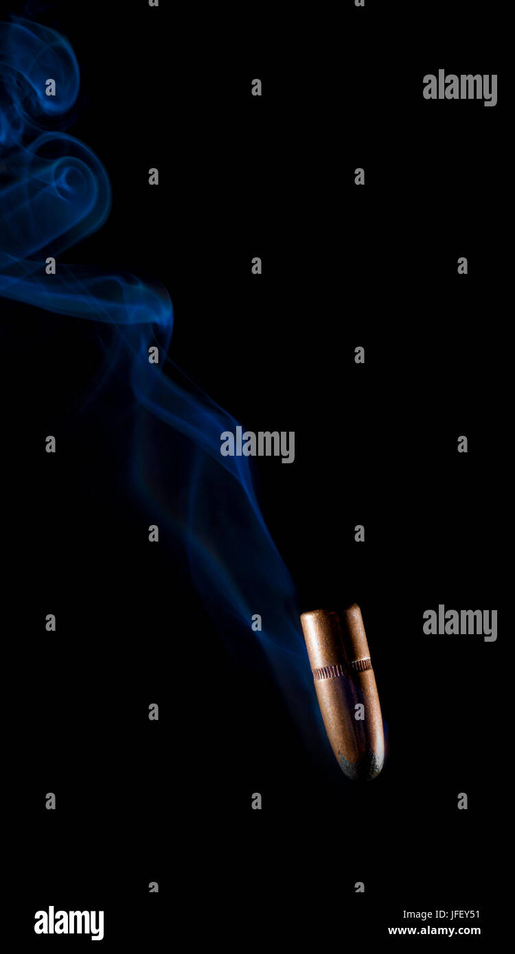 Copper plated bullet falling with blue smoke behind Stock Photo - Alamy