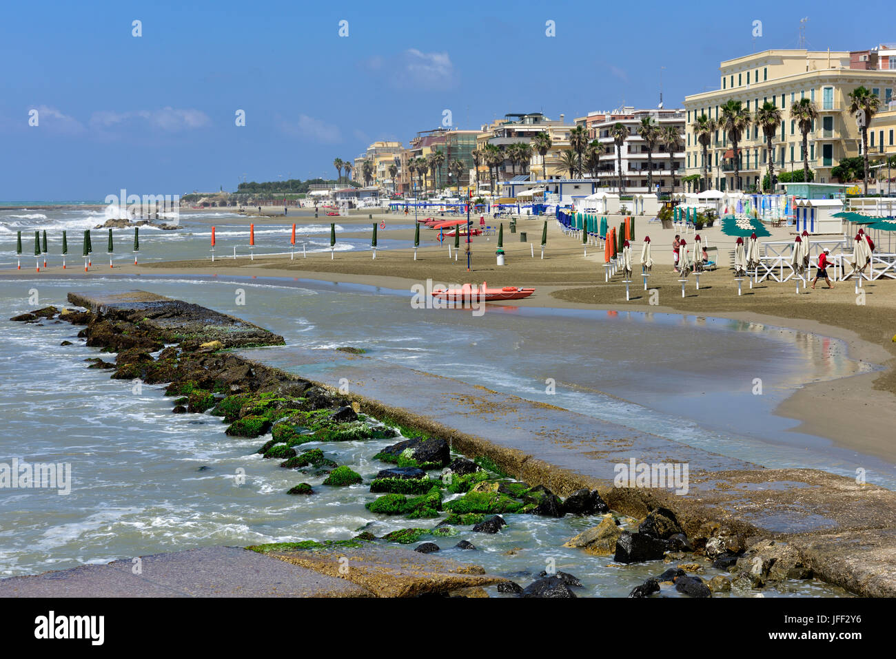 Nearly deserted beach with umbrellas and boats out on a windy summer ...