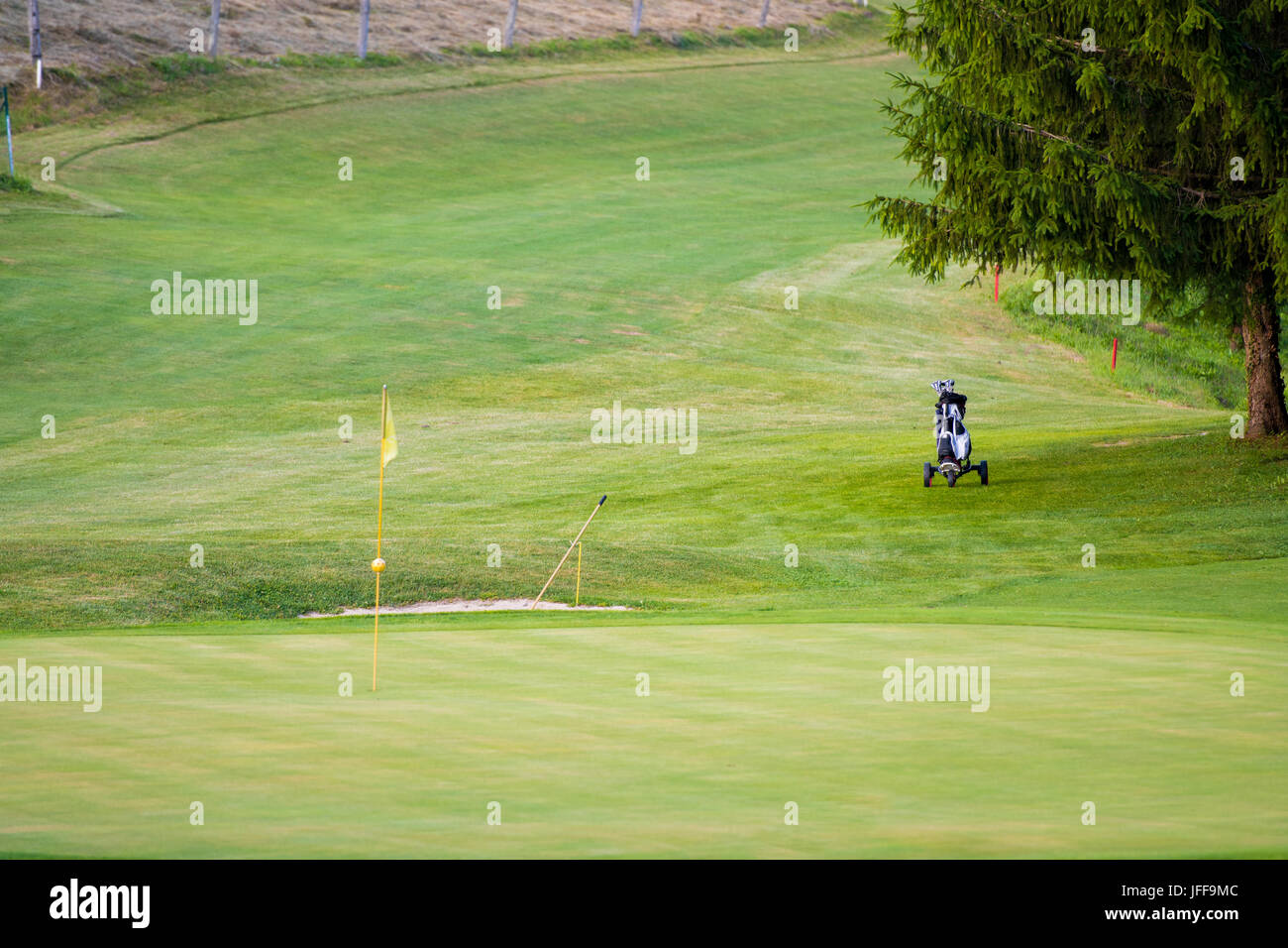 Golf course with one green with flag pole, a bunker and trolley on the ...