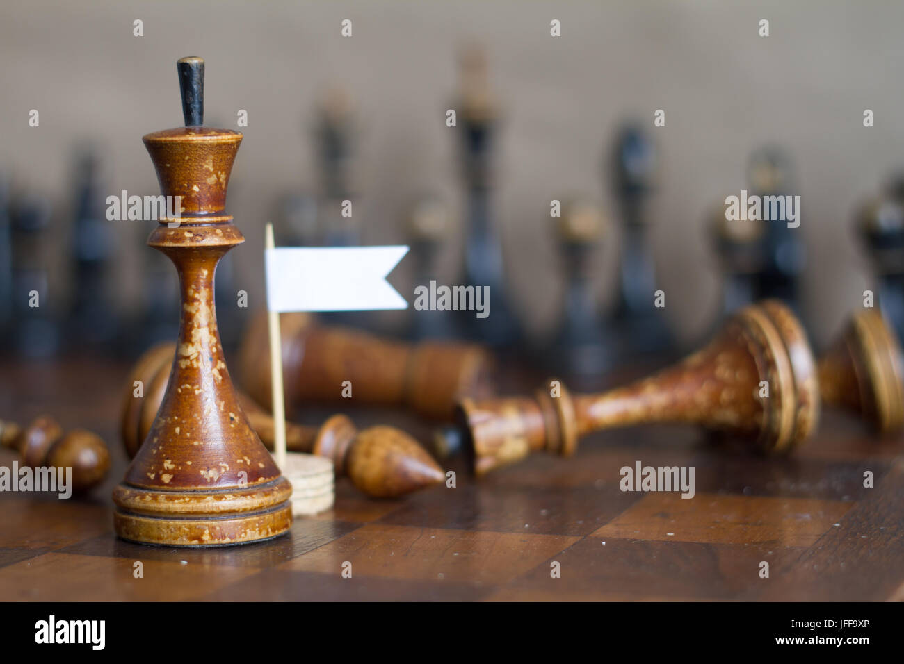 Ancient wooden chess pieces on an old chessboard. With the white flag ...