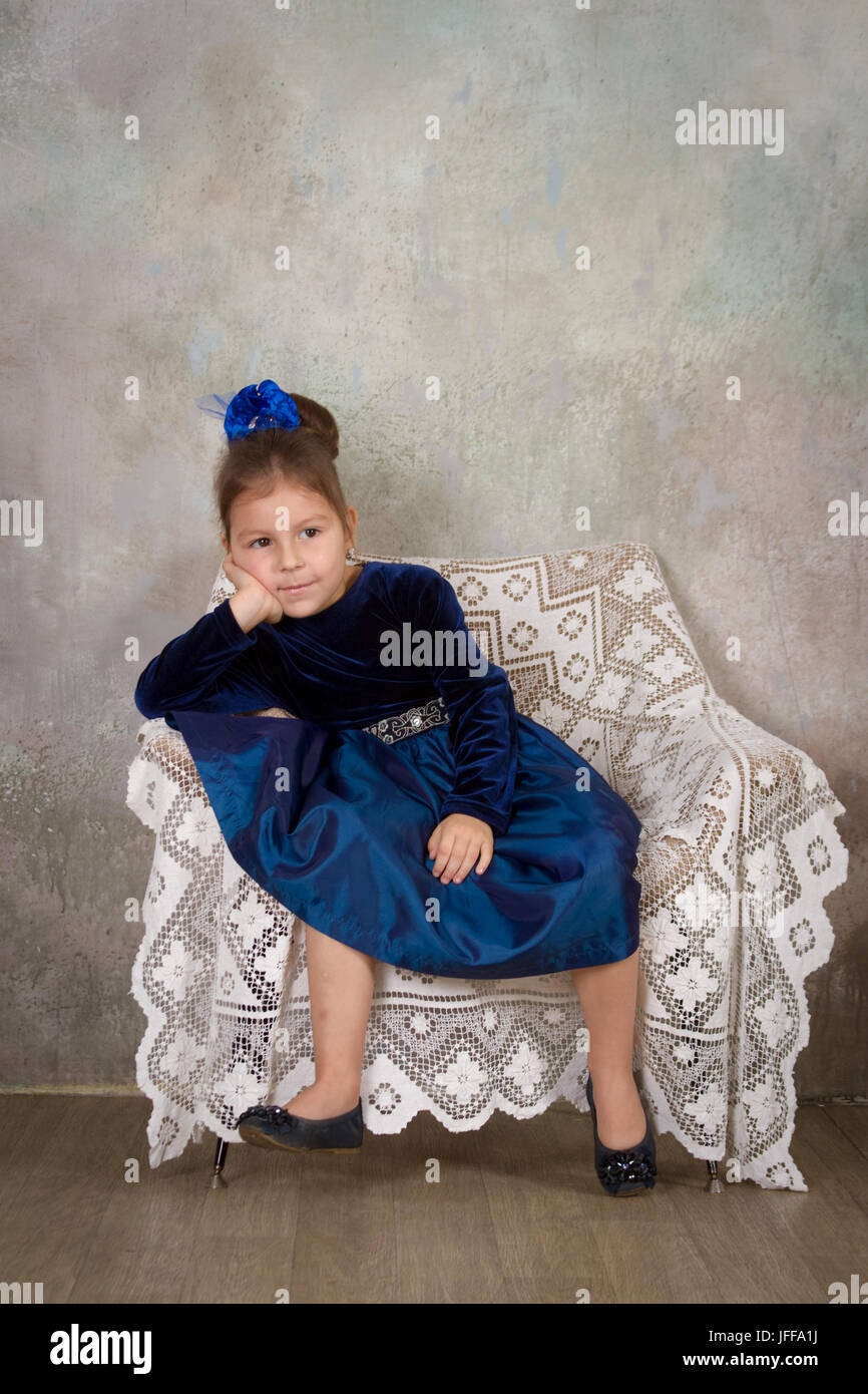 beautiful little girl princess in blue dress sitting on white chair and ...