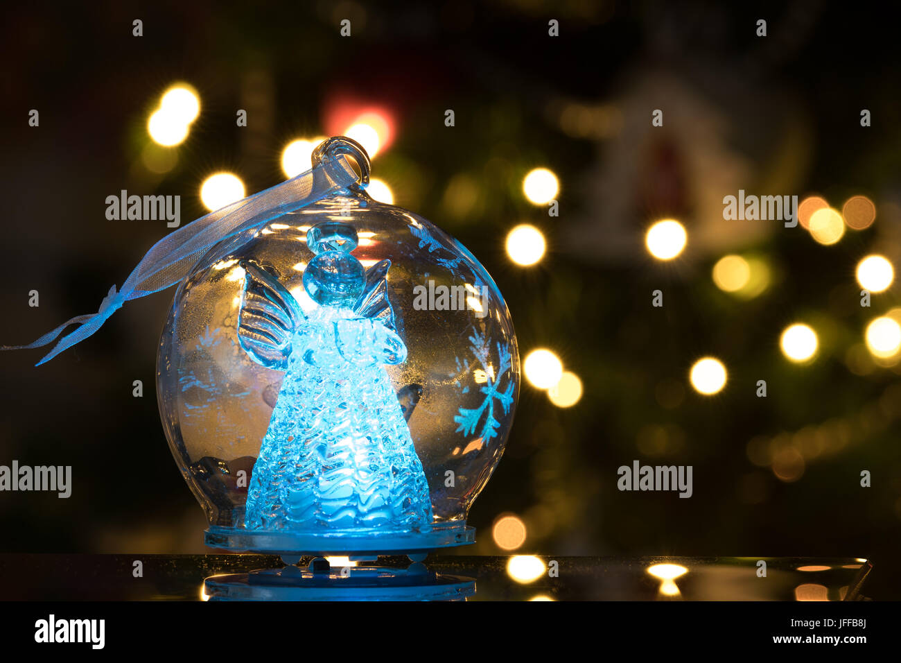 Illuminated angel figure in glass bulb, soft bokeh Christmas lights as ...