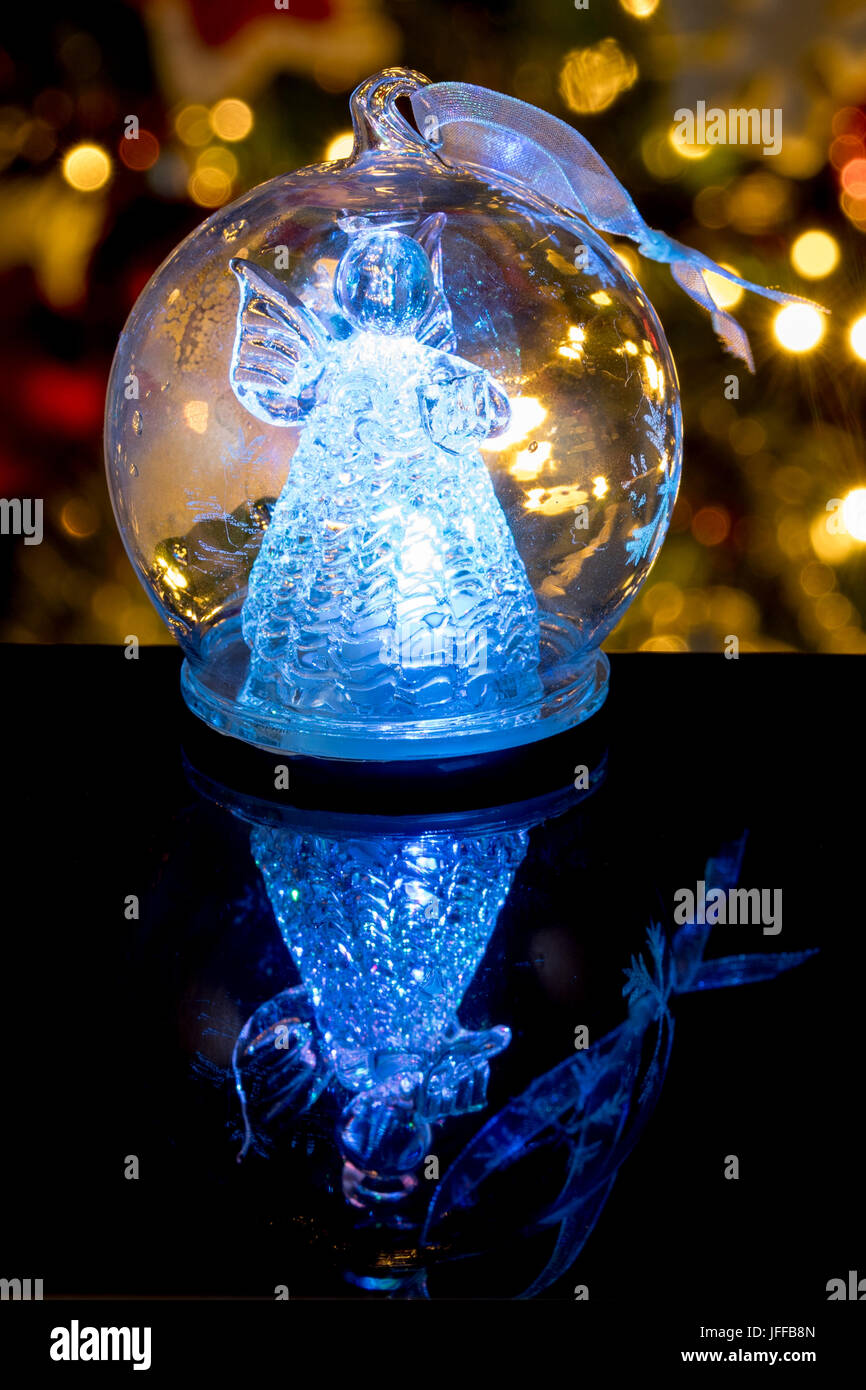 Illuminated angel figure in glass bulb, soft bokeh Christmas lights as ...