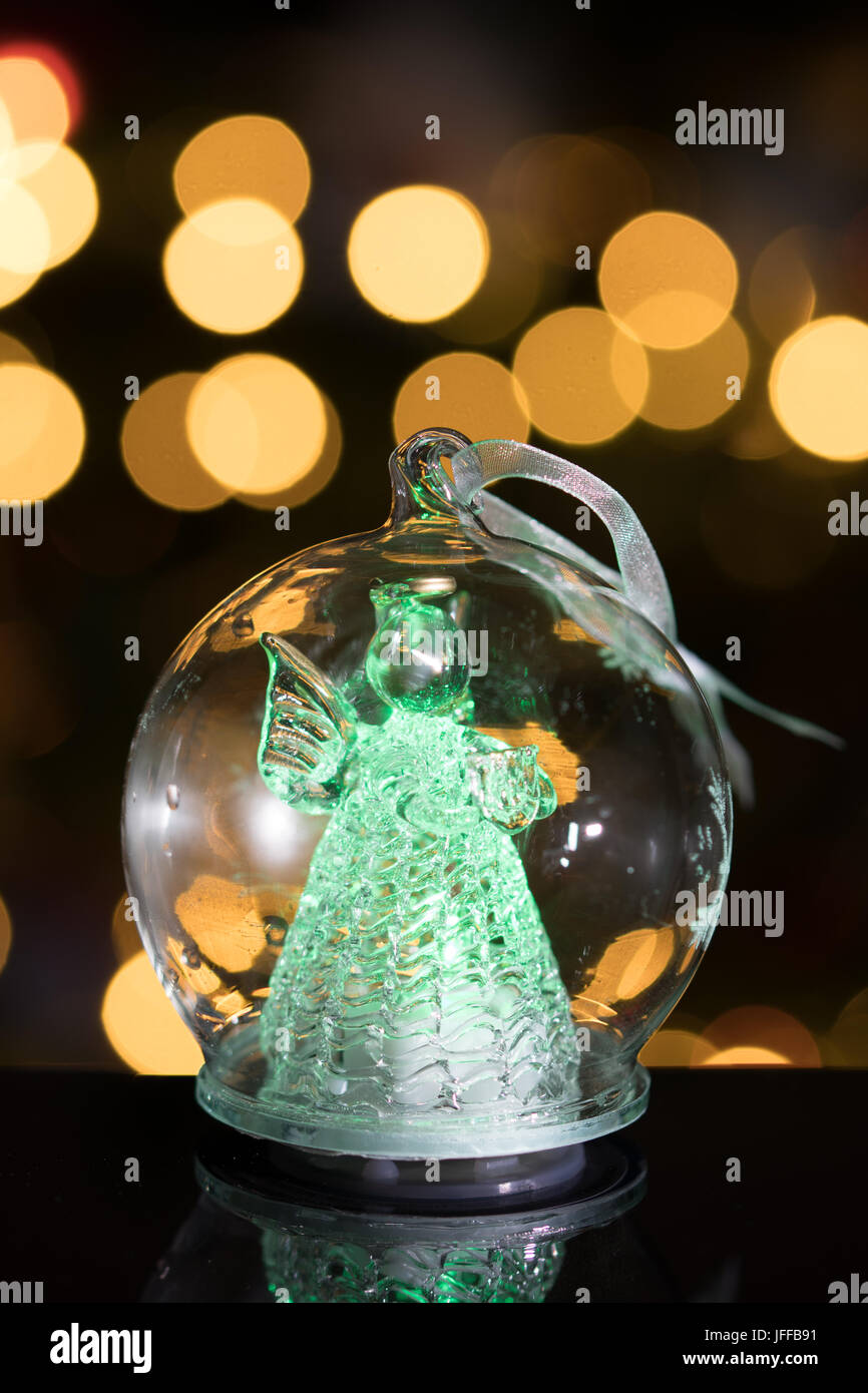 Illuminated angel figure in glass bulb, soft bokeh Christmas lights as ...