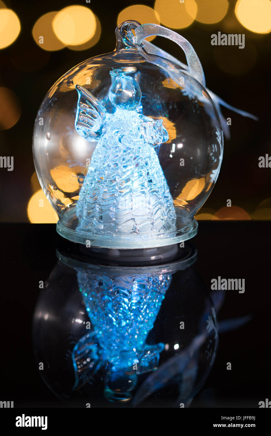 Illuminated angel figure in glass bulb, soft bokeh Christmas lights as ...