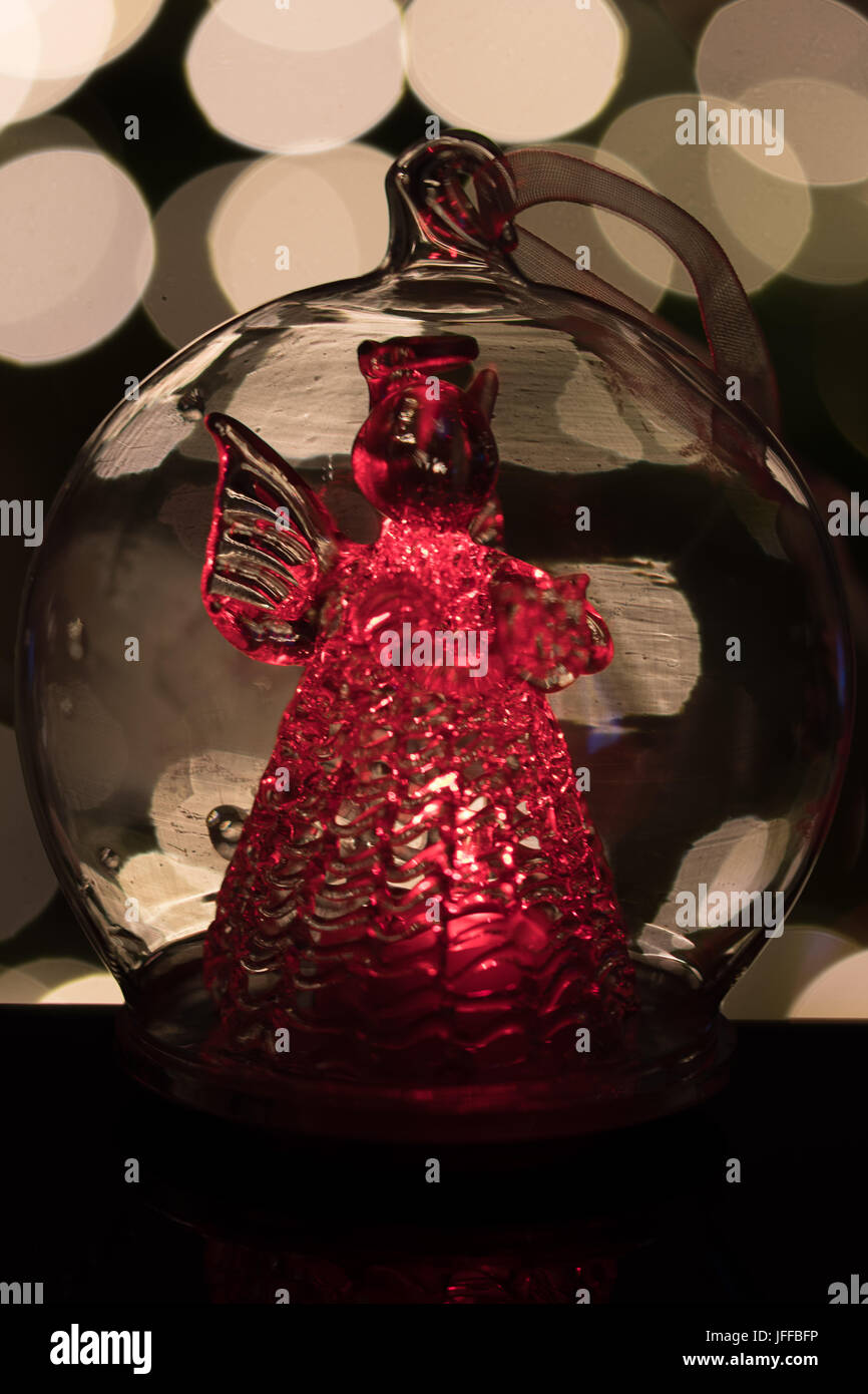 Illuminated angel figure in glass bulb, soft bokeh Christmas lights as ...
