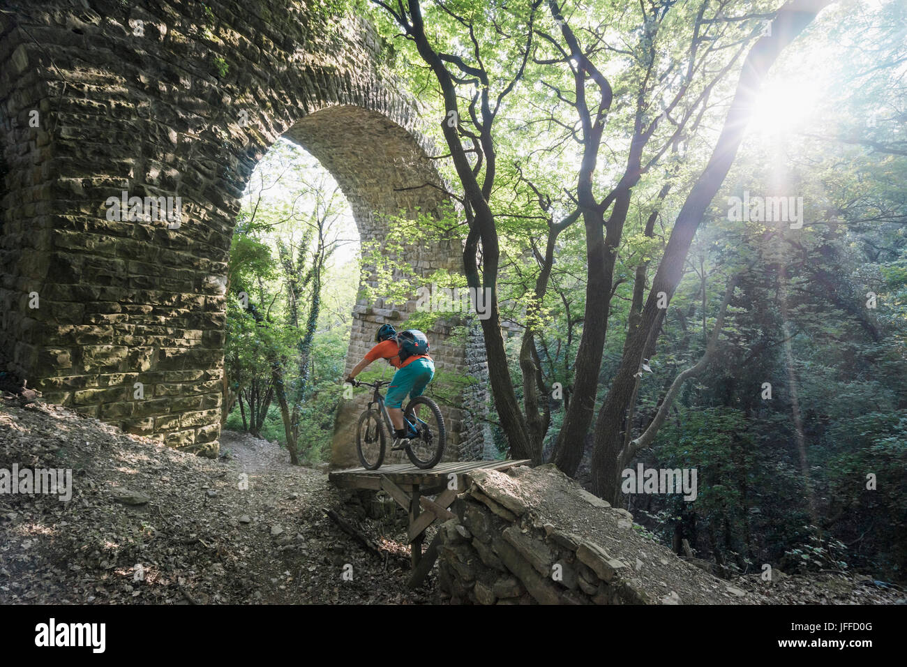 Man riding bike over footpath by arched stone wall in forest Stock ...