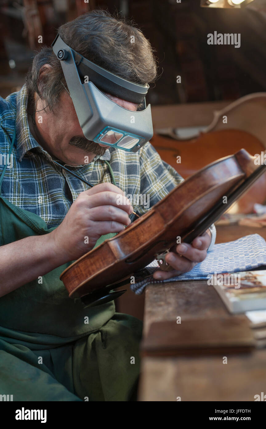 Violin maker using magnification for painting violin Stock Photo - Alamy