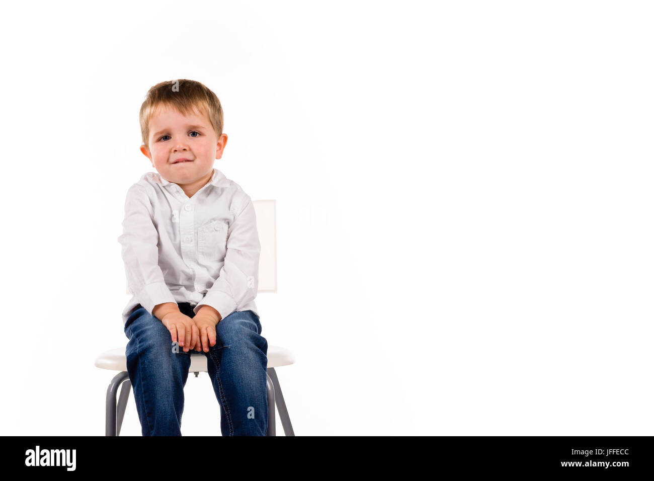 Adorable cute little boy sitting on a stool wearing a white shirt and a ...