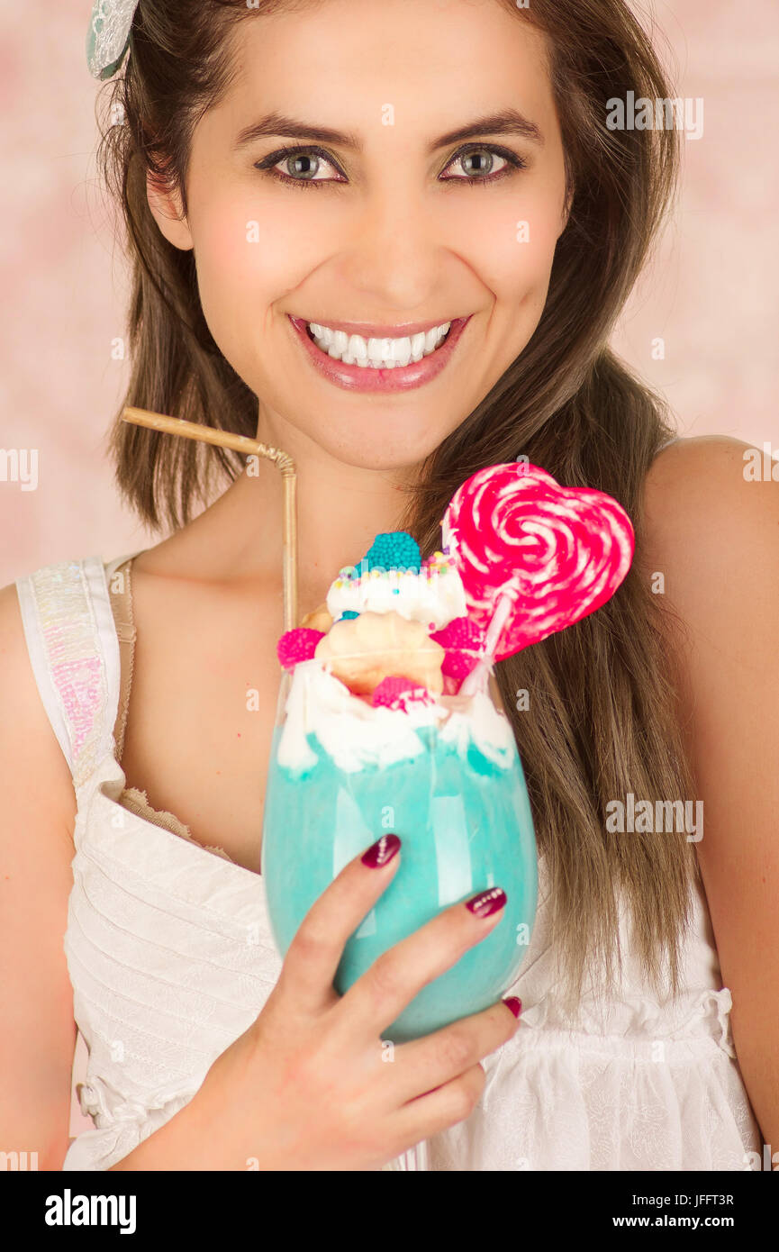 Smiling young beautiful woman with a tasty blue milk shake in studio ...