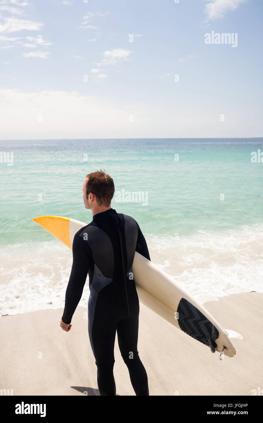 Rear view of surfer with surfboard standing on the beach Stock Photo ...