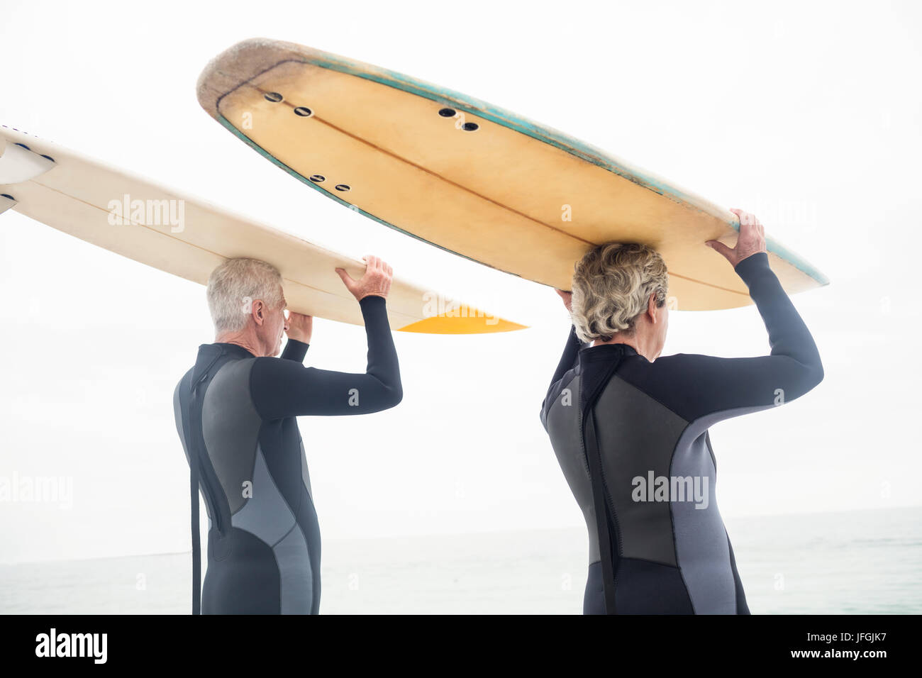 Senior couple in wetsuit carrying surfboard over head Stock Photo - Alamy