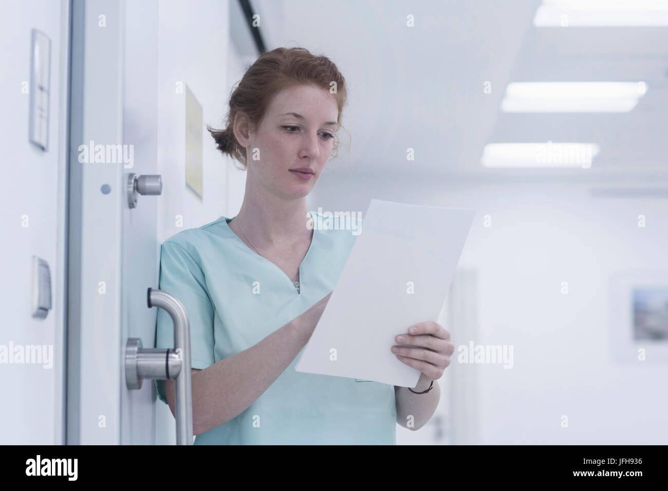 Young nurse reading medical charts while leaning by door Stock Photo ...