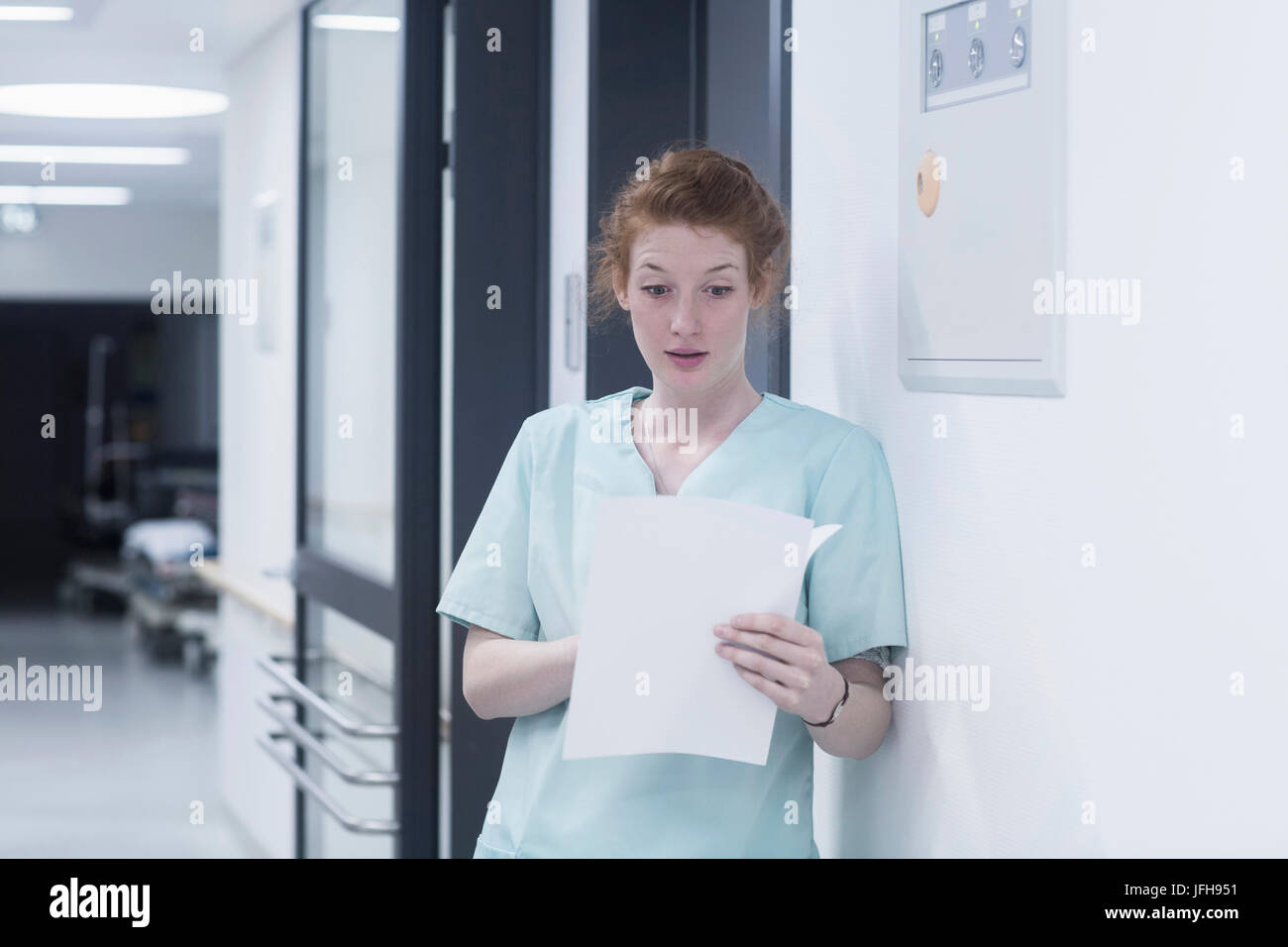 Shocked nurse reading medical chart while leaning by wall Stock Photo ...