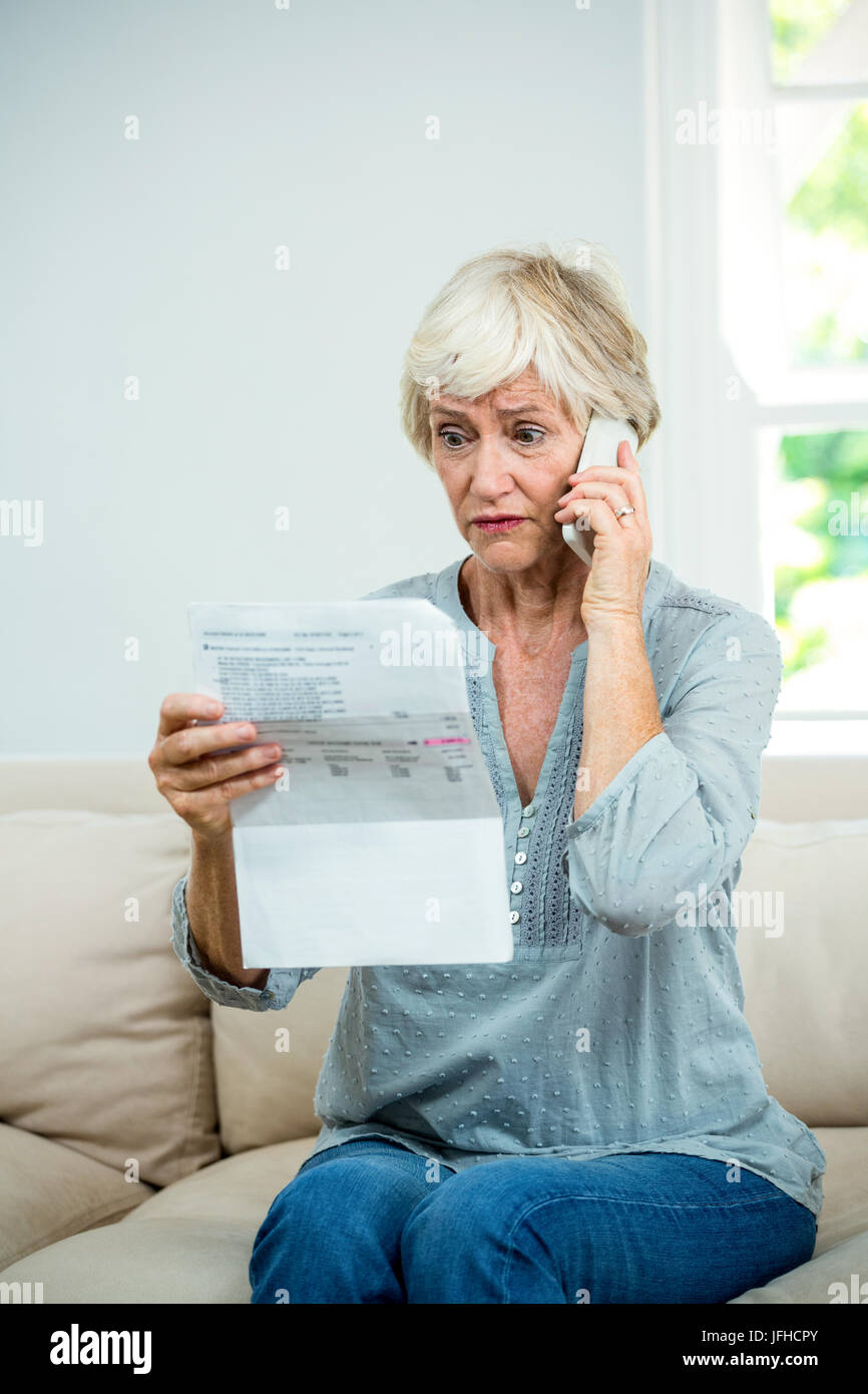 Aged woman reading document while talking on phone Stock Photo - Alamy