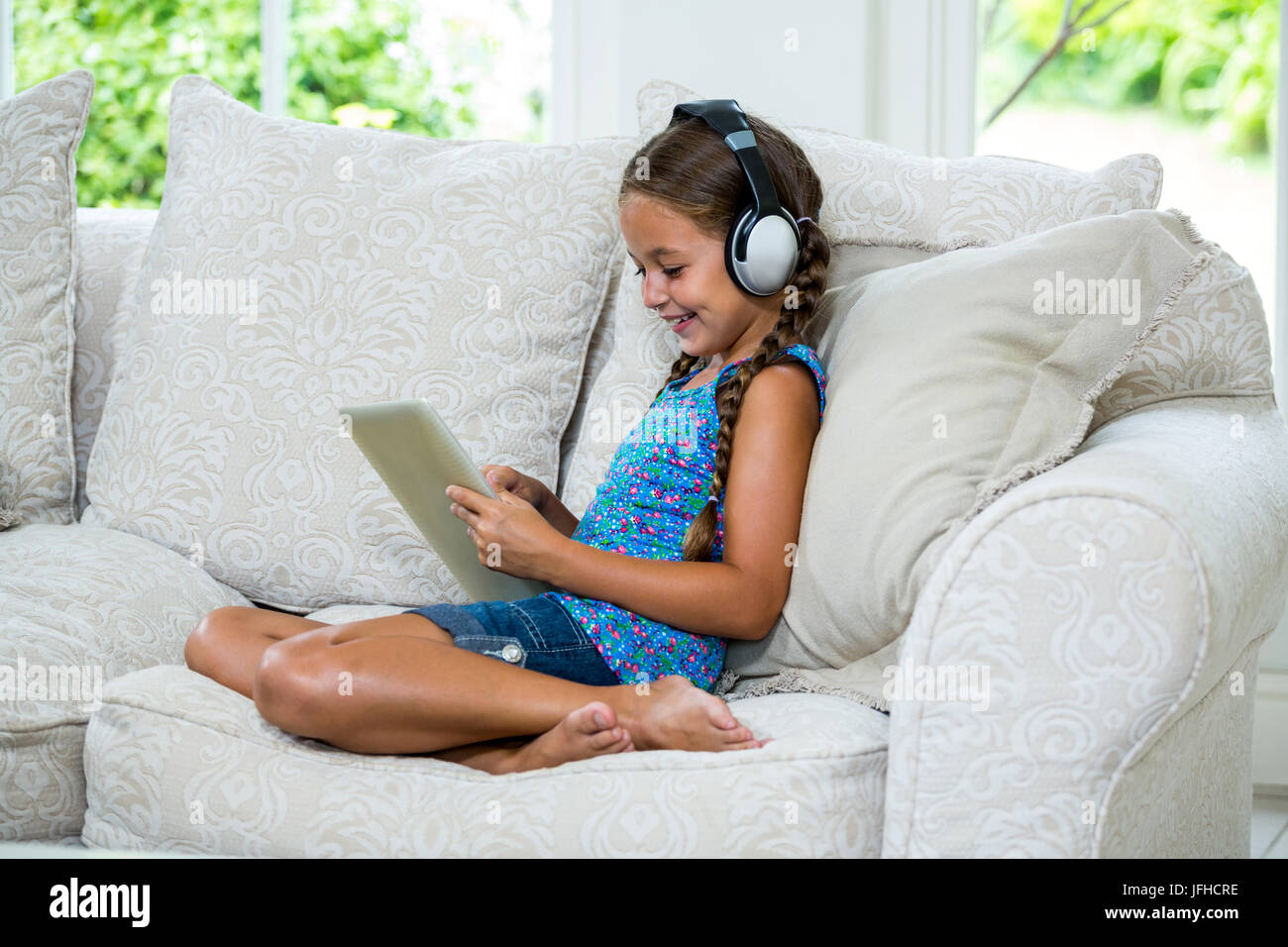 Girl using digital tablet while listening music on sofa Stock Photo - Alamy