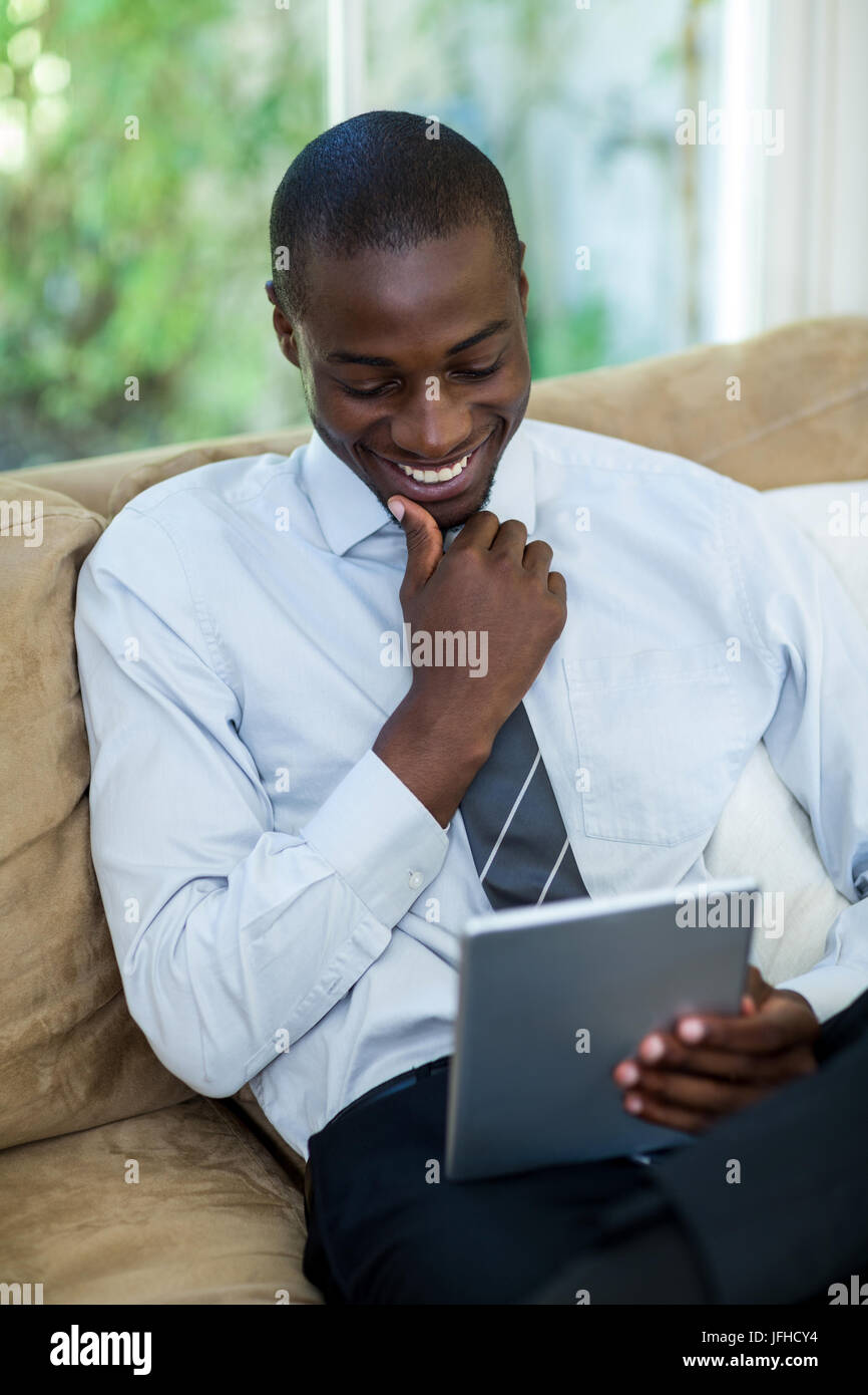 Young man sitting on sofa and using digital tablet Stock Photo - Alamy