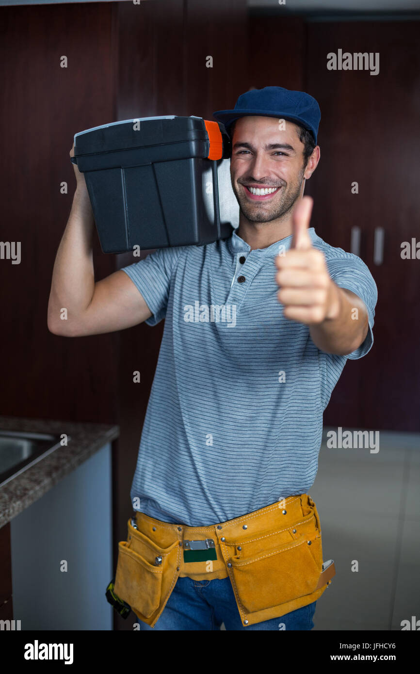 Smiling man carrying toolbox while showing thumbs up Stock Photo - Alamy