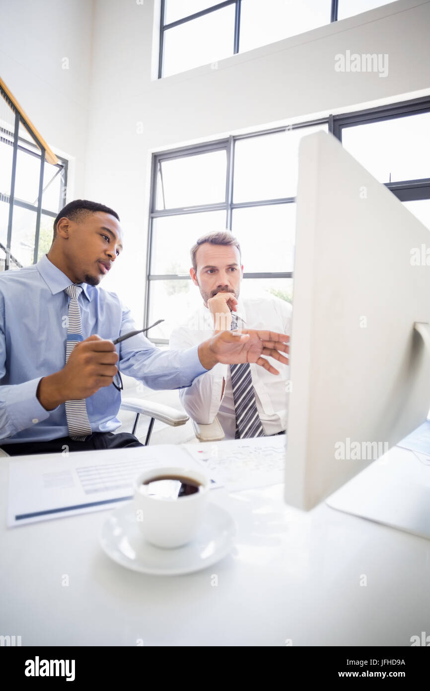 Businessmen looking at computer and interacting in office Stock Photo ...