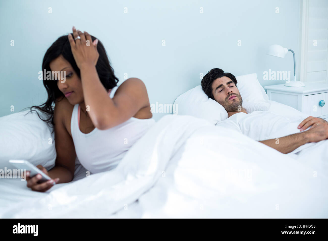 Woman checking her mobile phone while man sleeping on bed Stock Photo ...