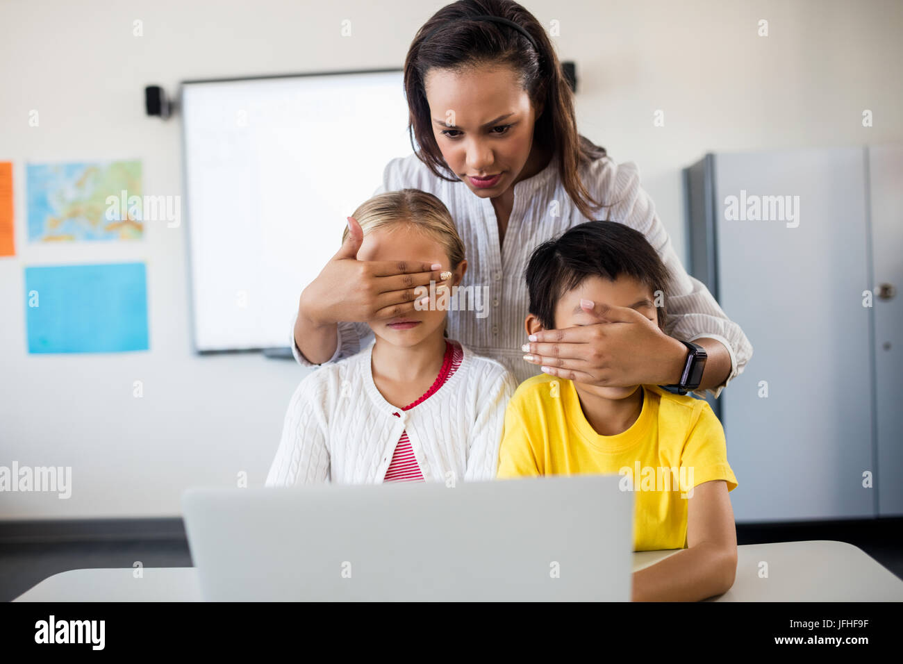 Teacher covering pupils eyes in front of computer Stock Photo - Alamy