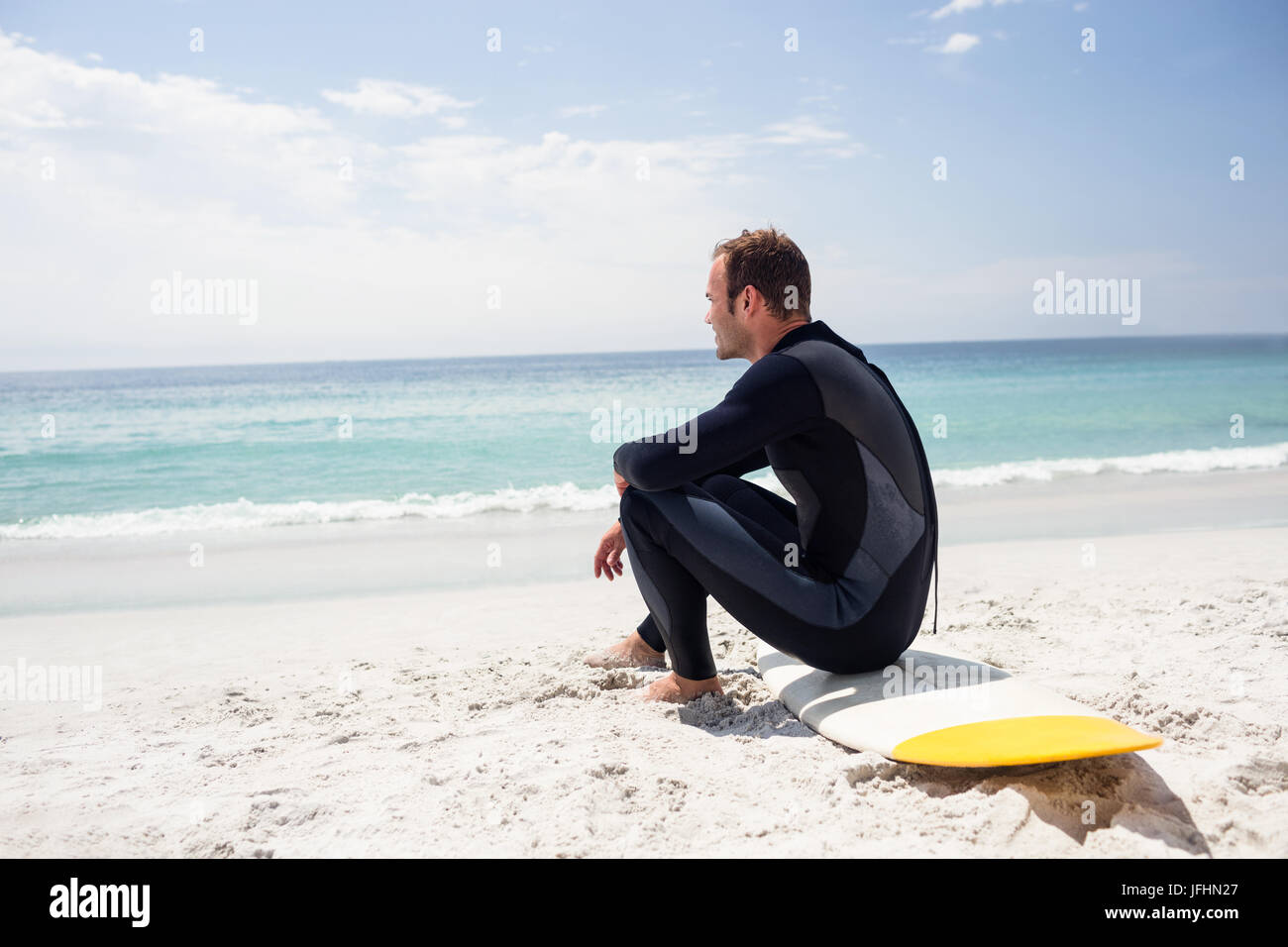 Happy surfer in wetsuit sitting with surfboard on the beach Stock Photo ...