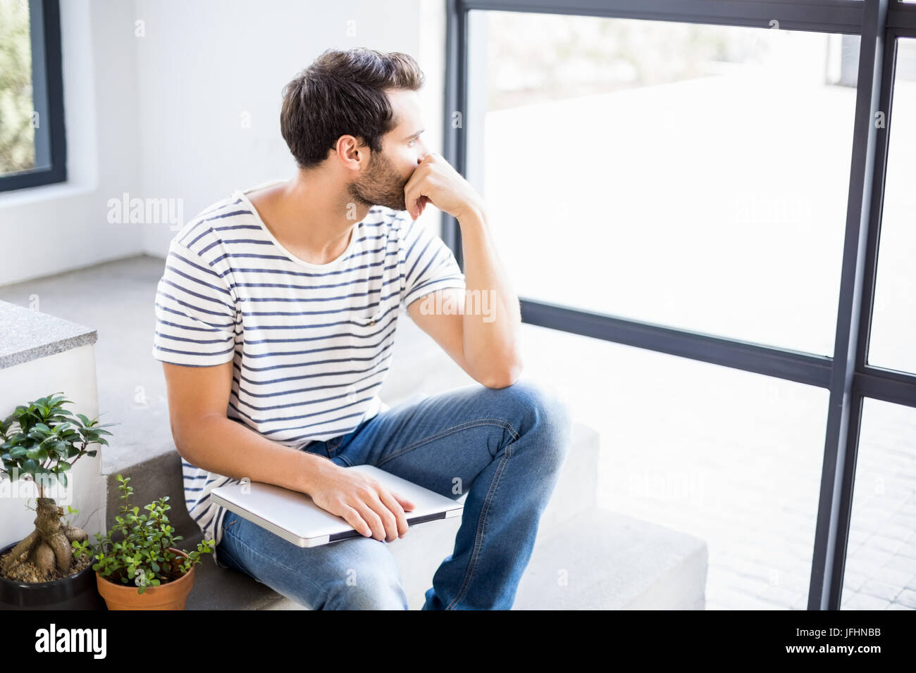 Man sitting with laptop looking out through window Stock Photo - Alamy